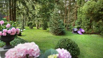 Jardim bem cuidado com diversas árvores, gramado e um vaso grande com flores cor-de-rosa.