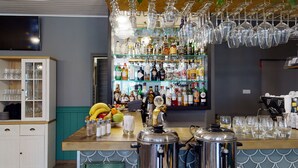 Uma área de bar com prateleiras de garrafas de bebidas, uma exposição de frutas e uma máquina de café.