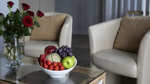 Sala de estar com mesa de vidro, uma tigela de frutas e rosas vermelhas.