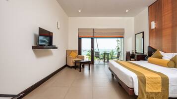 Quarto de hotel com cama, televisão, cadeira, mesa pequena e varanda com vista para o oceano.