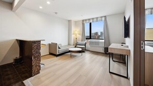 Uma sala de estar moderna com um sofá, uma mesa redonda pequena, uma luminária e vista da cidade através de grandes janelas.