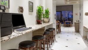Uma cozinha moderna com bancada de mármore, um laptop e banquetas de bar. Há plantas em vasos e quadros na parede.