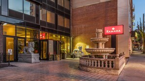 Um edifício com a placa 'RAMADA', uma estátua de leão de pedra e uma fonte.