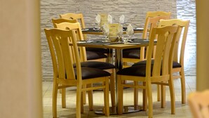 Uma sala de jantar com parede de pedra, cadeiras de madeira e mesa posta para quatro pessoas.