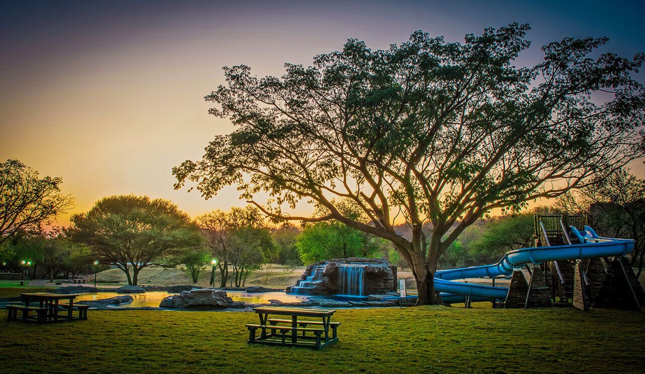 Um parque com mesas para piquenique, parquinho e uma cascata.