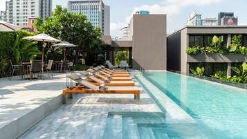 Piscina no terraço com espreguiçadeiras e guarda-sóis, cercada por vegetação e edifícios modernos.