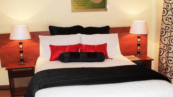 Quarto de hotel com cama, duas mesas de cabeceira, duas luminárias, um aviso na parede e uma cortina.