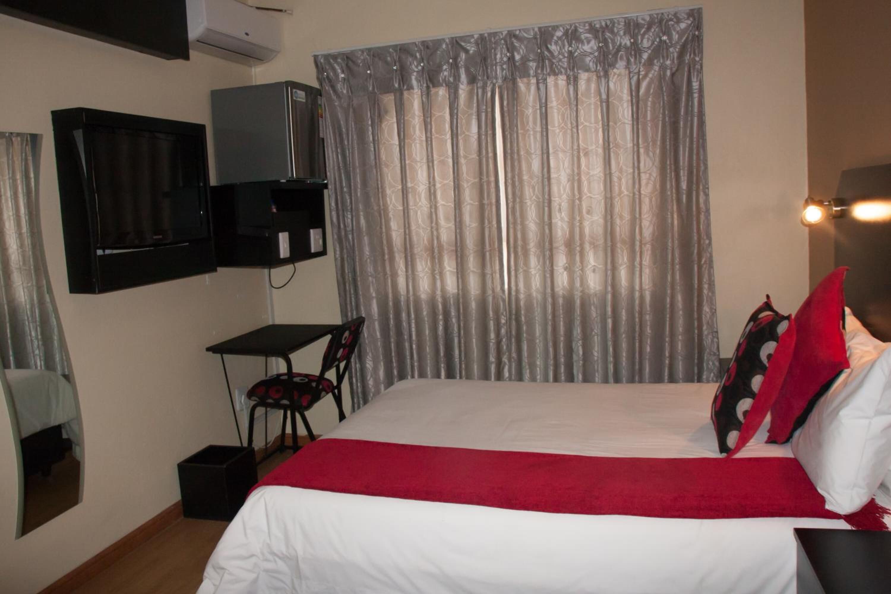 Quarto de hotel com cama, escrivaninha, cadeira, televisão e cortina.