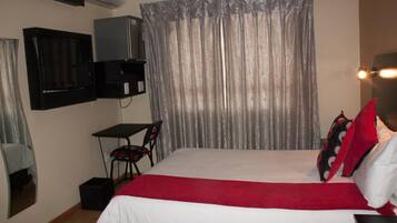 Quarto de hotel com cama, escrivaninha, cadeira, televisão e cortina.