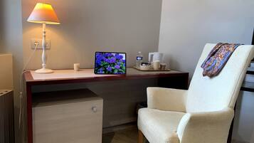 Quarto de hotel com escrivaninha, cadeira, luminária, laptop, e uma mesinha com garrafa de água, xícara de café e caixa de lenços.