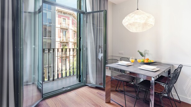 Uma sala de jantar com mesa, cadeiras, luminária pendente e vista para uma varanda externa através de uma porta de vidro.