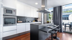 Cozinha moderna com eletrodomésticos de aço inoxidável, uma ilha central com banquetas e vista para o exterior através de grandes janelas.