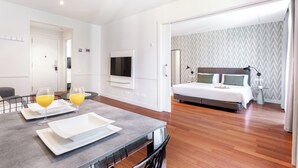 Quarto de hotel moderno com área de jantar, cama e televisão.