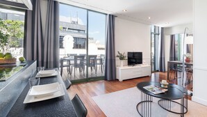 Uma sala de estar moderna com área de jantar, janelas amplas, televisão de tela plana e vista para a cidade.