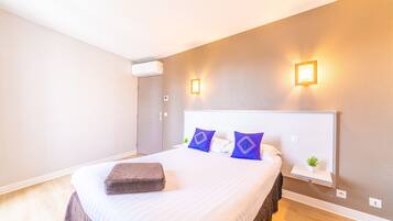 Quarto de hotel com cama, mesa de cabeceira, ar condicionado fixado na parede e duas arandelas.