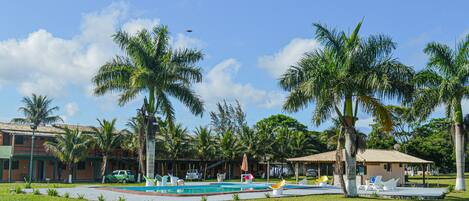 Uma área de piscina com palmeiras, um pequeno edifício e um carro.