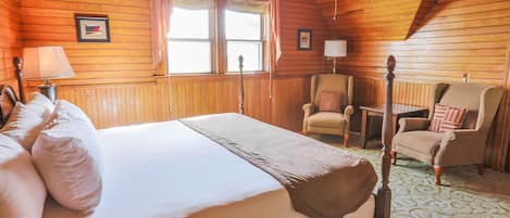 Um quarto aconchegante com uma cama grande, uma cadeira, uma mesa e uma janela com cortinas.
