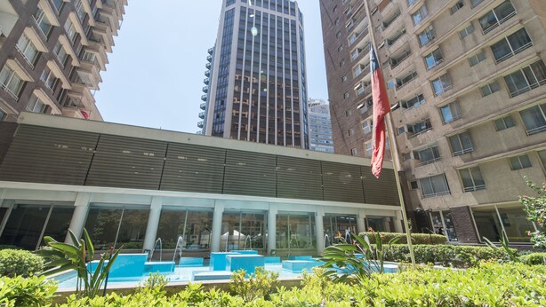 Um edifício moderno com área de piscina, rodeado por edifícios residenciais altos.