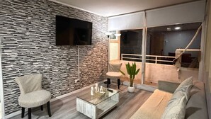 Uma sala de estar moderna com parede estampada em pedra, televisão de tela plana, mesa de centro de vidro, sofá bege e planta em vaso.
