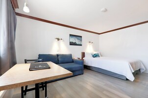 Quarto de hotel com cama, sofá azul, mesa de madeira e duas luzes fixadas na parede.