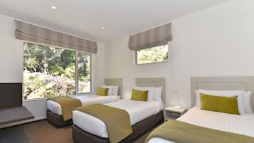 Quarto de hotel com duas camas, janelas amplas e vista para o verde.