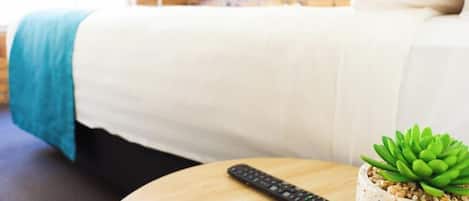 Quarto com uma cama, um controle remoto e um vaso de planta sobre uma mesa redonda.