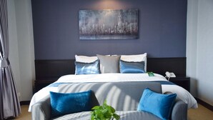 Quarto de hotel com cama, mesa de cabeceira, planta e uma obra de arte com vista para a cidade.
