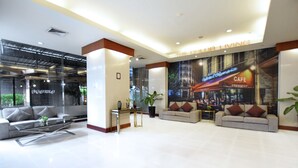 Um lobby moderno com um mural grande, dois sofás, uma mesa de centro e um balcão de recepção.