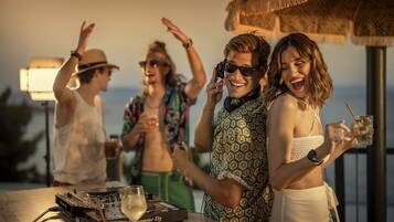 Um grupo de pessoas aproveitando bebidas e música em um evento na praia, com equipamento de DJ.