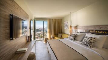 Quarto de hotel moderno com uma cama grande, televisão de tela plana, varanda com vista e um aviso na cabeceira com a inscrição "EJAKAI PLACES".