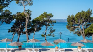 Área de piscina com espreguiçadeiras e guarda-sóis, com vista para um mar azul e límpido.