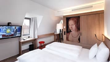 Quarto de hotel com cama, escrivaninha, televisão e janela.