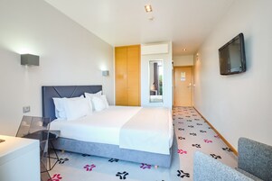 Quarto de hotel moderno com uma cama grande, uma escrivaninha, televisão de tela plana e carpete estampado.