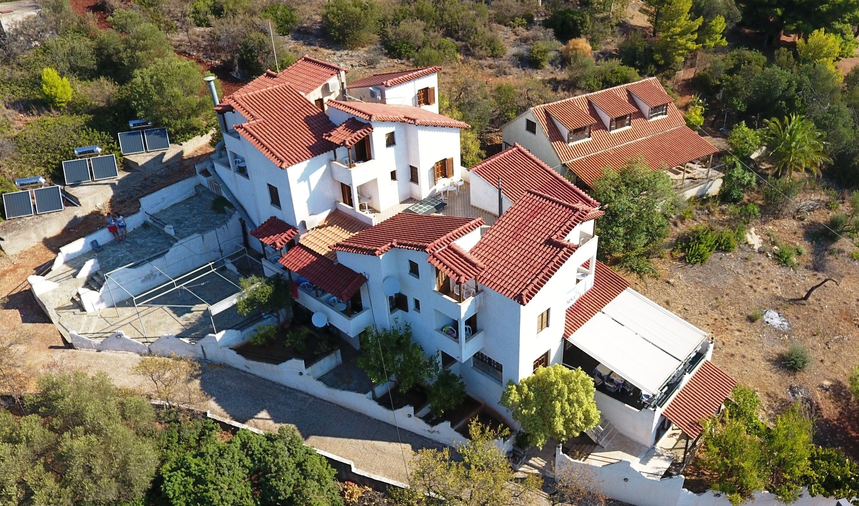 Um edifício grande e branco com telhados em telhas vermelhas, várias varandas e painéis solares.
