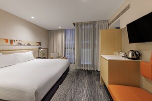 Quarto de hotel com uma cama grande, uma escrivaninha com cadeira, televisão e janela com cortinas.