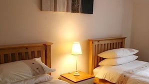 Uma cama de casal com cabeceira de madeira, uma mesa de cabeceira com abajur e um criado-mudo com gaveta.