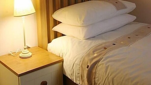 Uma cama bem arrumada com cabeceira de madeira, abajur e mesa de cabeceira com gaveta.