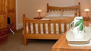 Uma cama de madeira com duas luminárias de cabeceira, um criado-mudo de madeira e uma bandeja com uma caneca e uma colher.