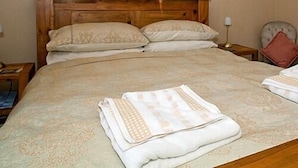 Uma cama bem arrumada com cabeceira de madeira, dois travesseiros e um cobertor dobrado sobre ela.