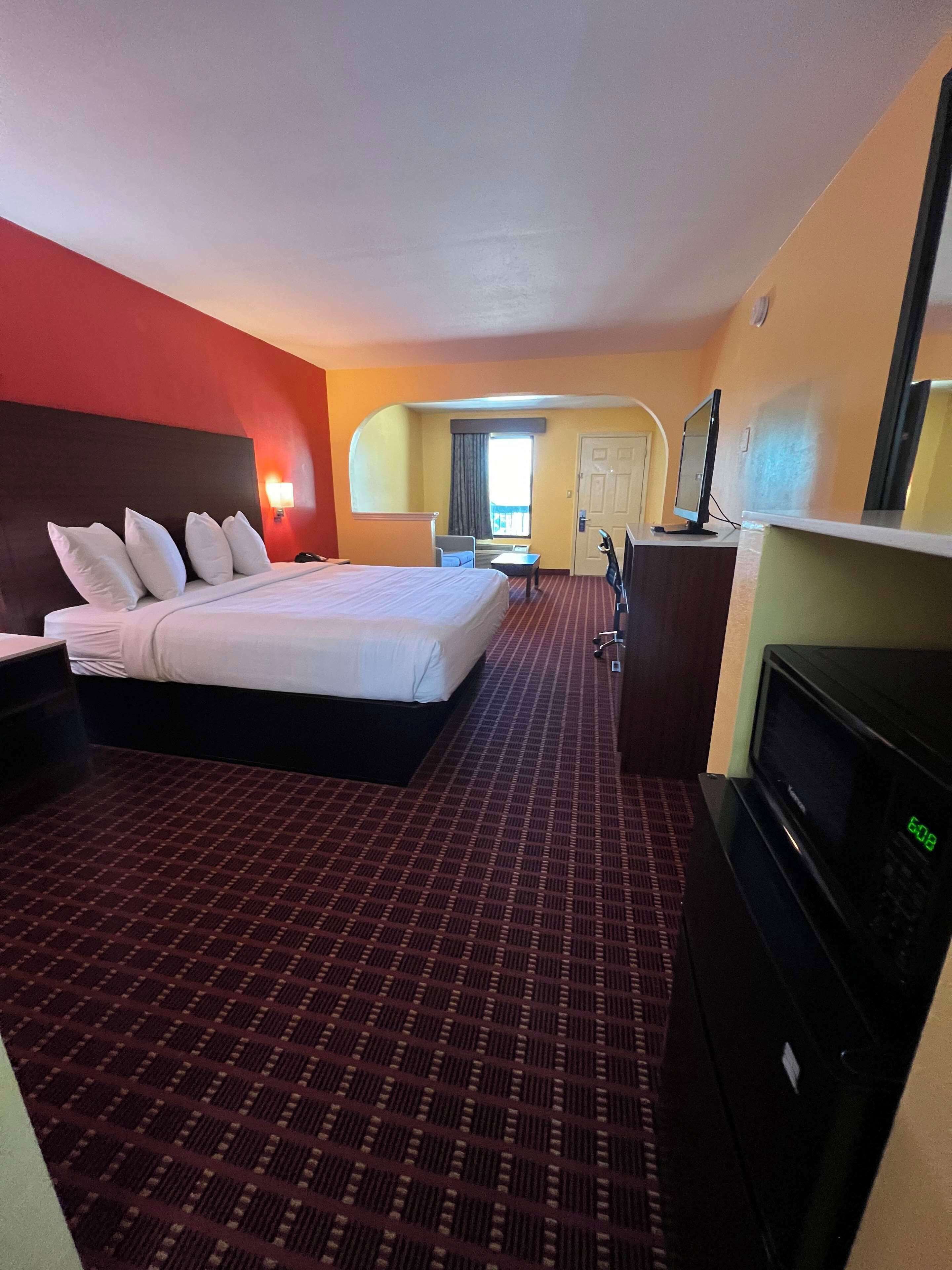 Quarto de hotel com uma cama grande, uma escrivaninha, uma televisão e uma janela com cortinas.