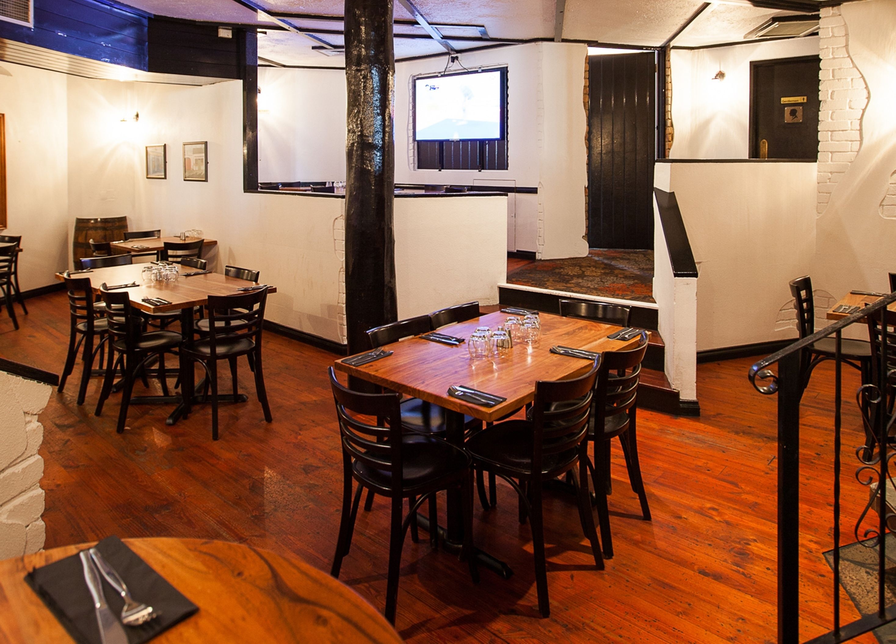 Um restaurante com mesas e cadeiras de madeira, uma tela de televisão e uma parede de tijolos.
