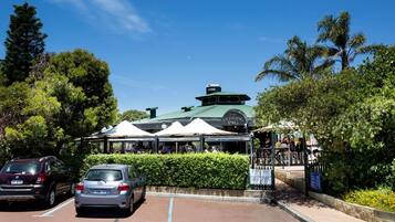 Restaurante com mesas ao ar livre, telhado verde e placa com o texto 'The Swinging Pig'.