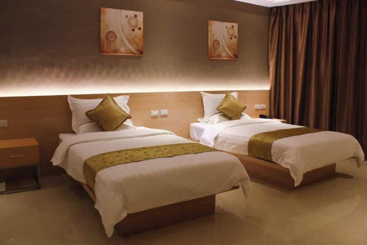 Quarto de hotel com duas camas, uma cabeceira de madeira e obras de arte na parede.