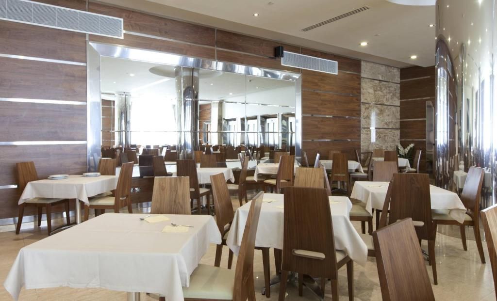 Uma ampla sala de jantar com várias mesas e cadeiras, janelas grandes e um design de interiores moderno.
