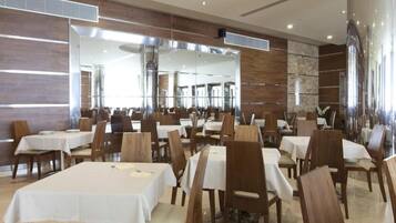 Uma ampla sala de jantar com várias mesas e cadeiras, janelas grandes e um design de interiores moderno.