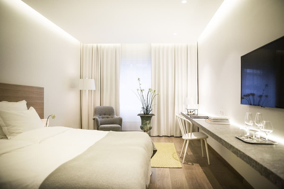 Quarto de hotel com cama, escrivaninha, cadeira, televisão e planta em vaso.