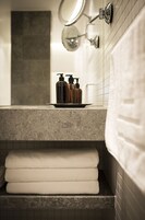 Casa de banho com bancada de mármore, espelho, porta-toalhas e uma prateleira com artigos de higiene pessoal.