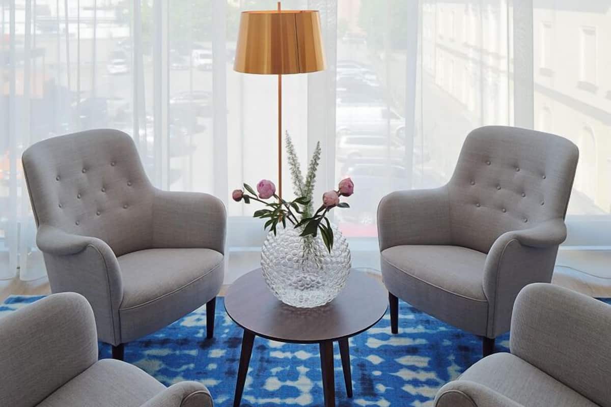 Um quarto com duas poltronas cinzentas, uma mesa redonda pequena com um vaso de flores e um abajur.