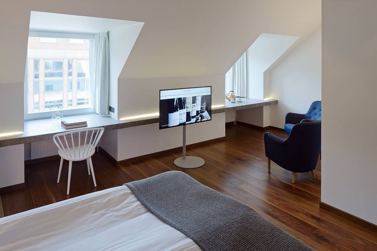 Quarto moderno com cama grande, escrivaninha com computador, uma cadeira e televisão.