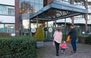 Entrada do Grand Hotel Amstelveen com portas de vidro, acesso coberto e uma placa acima.